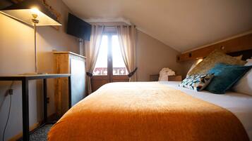 Quarto de hotel com cama, escrivaninha, abajur e televisão na parede.