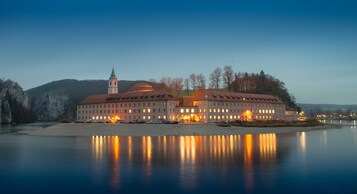 Um edifício grande e histórico com uma torre imponente, localizado às margens de águas calmas que refletem suas luzes.