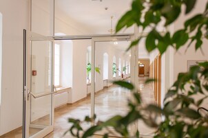 Um corredor com portas de vidro, plantas em vasos e chão de azulejos.