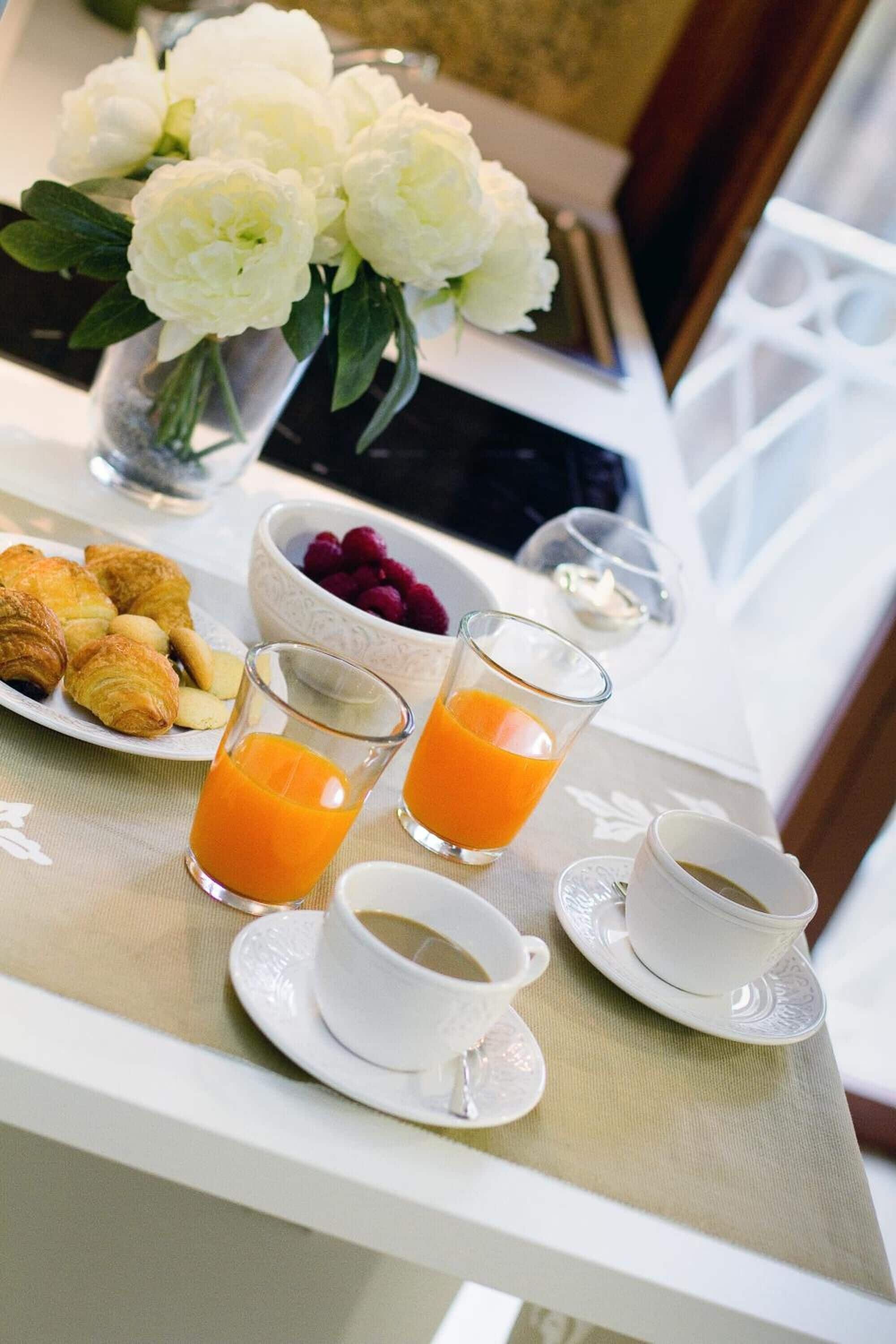 Uma mesa com disposição para o café da manhã, incluindo croissants, frutas vermelhas, suco de laranja e café.
