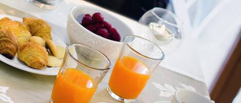 Uma mesa com disposição para o café da manhã, incluindo croissants, frutas vermelhas, suco de laranja e café.