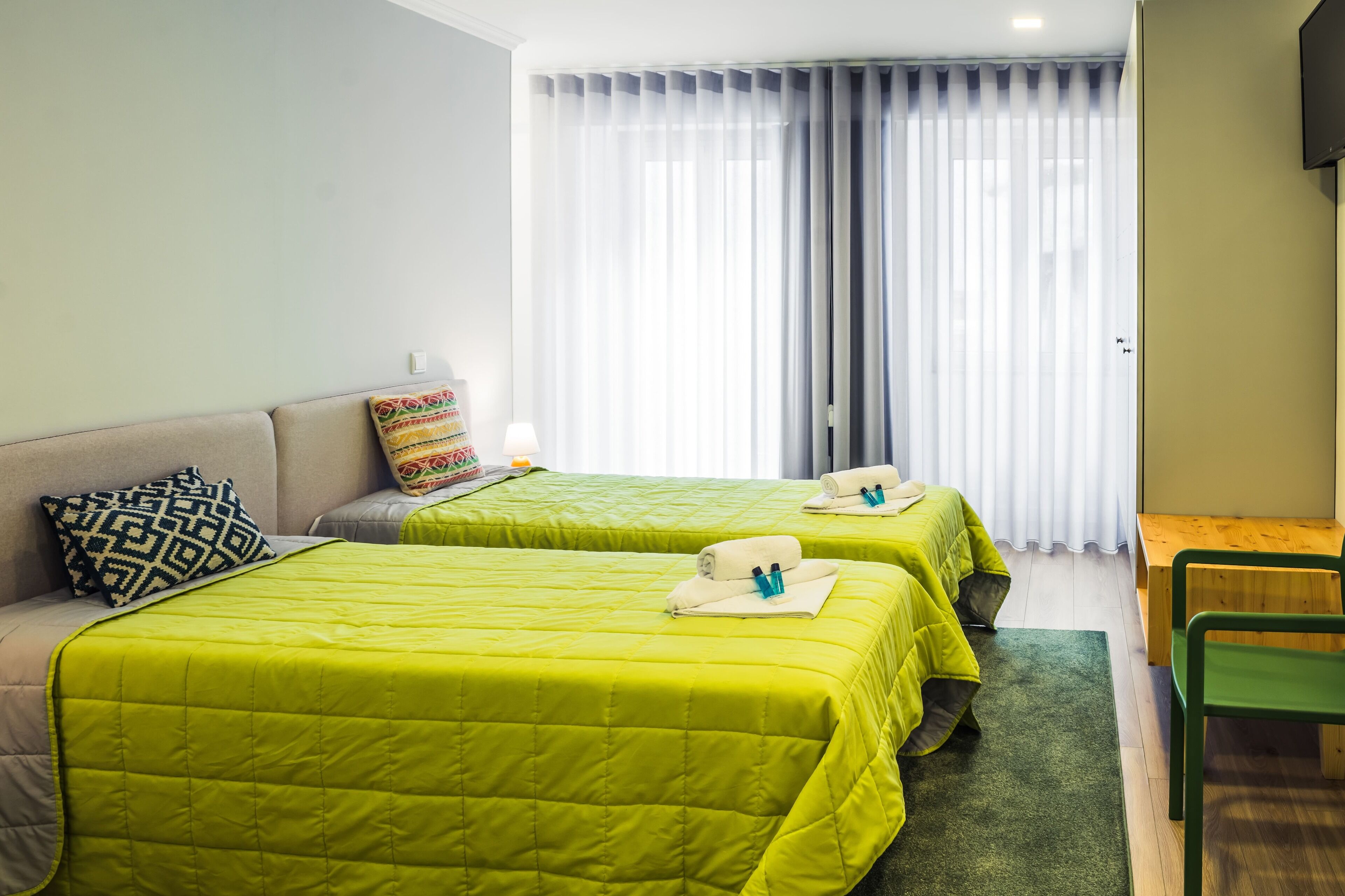 Quarto de hotel com duas camas, um sofá, uma mesa de madeira e uma cadeira verde.