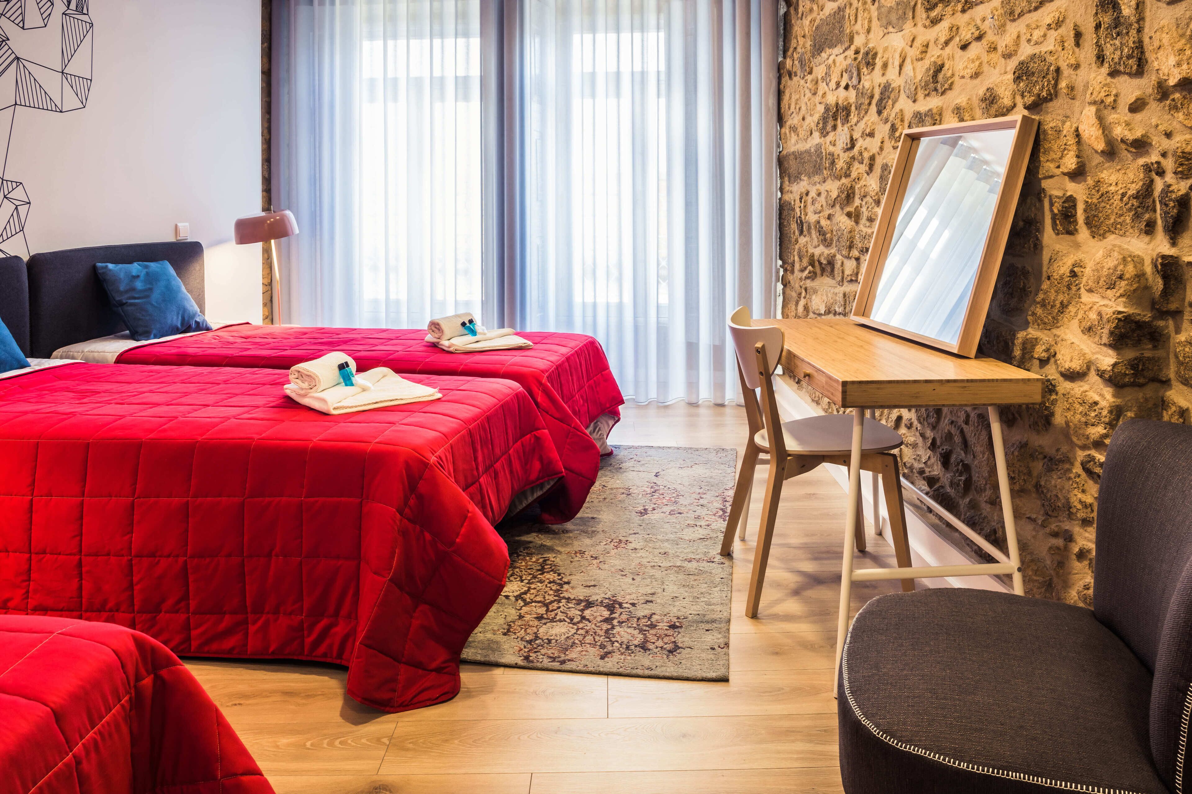 Quarto de hotel com duas camas, uma escrivaninha, uma cadeira e uma parede de pedra.