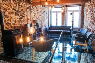 Uma sala de estar moderna com parede de pedra, uma mesa de centro de vidro, um sofá e duas poltronas.