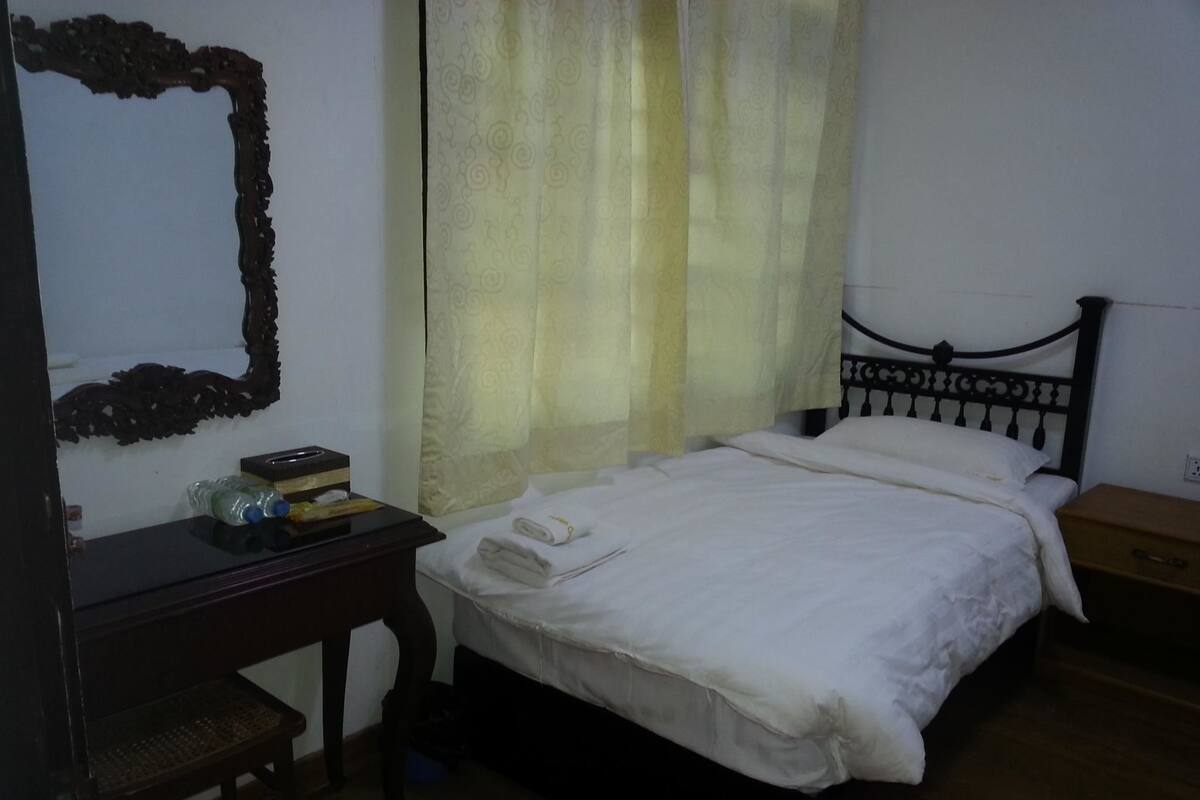 Quarto com cama, mesa de cabeceira, espelho e cortina.