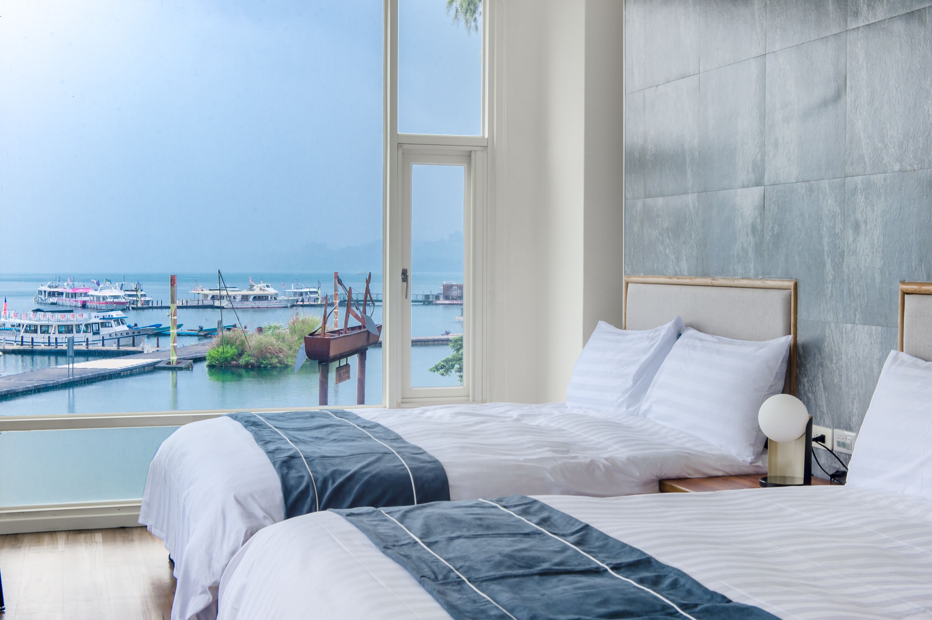 Quarto de hotel com uma janela ampla vista para um porto com barcos e um cais.