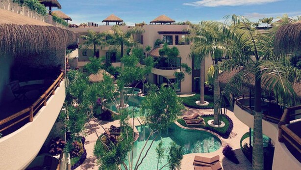 Um resort com piscina central, palmeiras e estruturas com telhado de palha.
