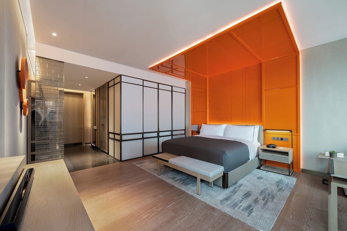 Quarto moderno com uma cama grande, um banco, uma mesa de cabeceira e um guarda-roupa.