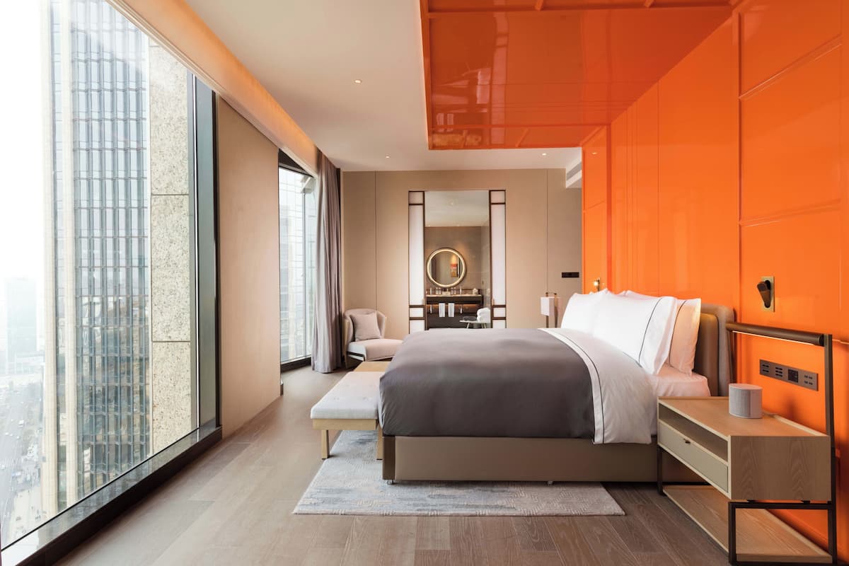Quarto moderno com cama grande, mesa de cabeceira, cadeira, escrivaninha e uma janela ampla.
