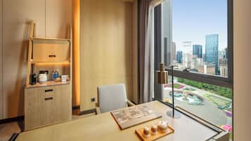Quarto de hotel com vista para a cidade, uma escrivaninha com um laptop, uma cadeira, um armário de madeira e uma janela com cortinas.