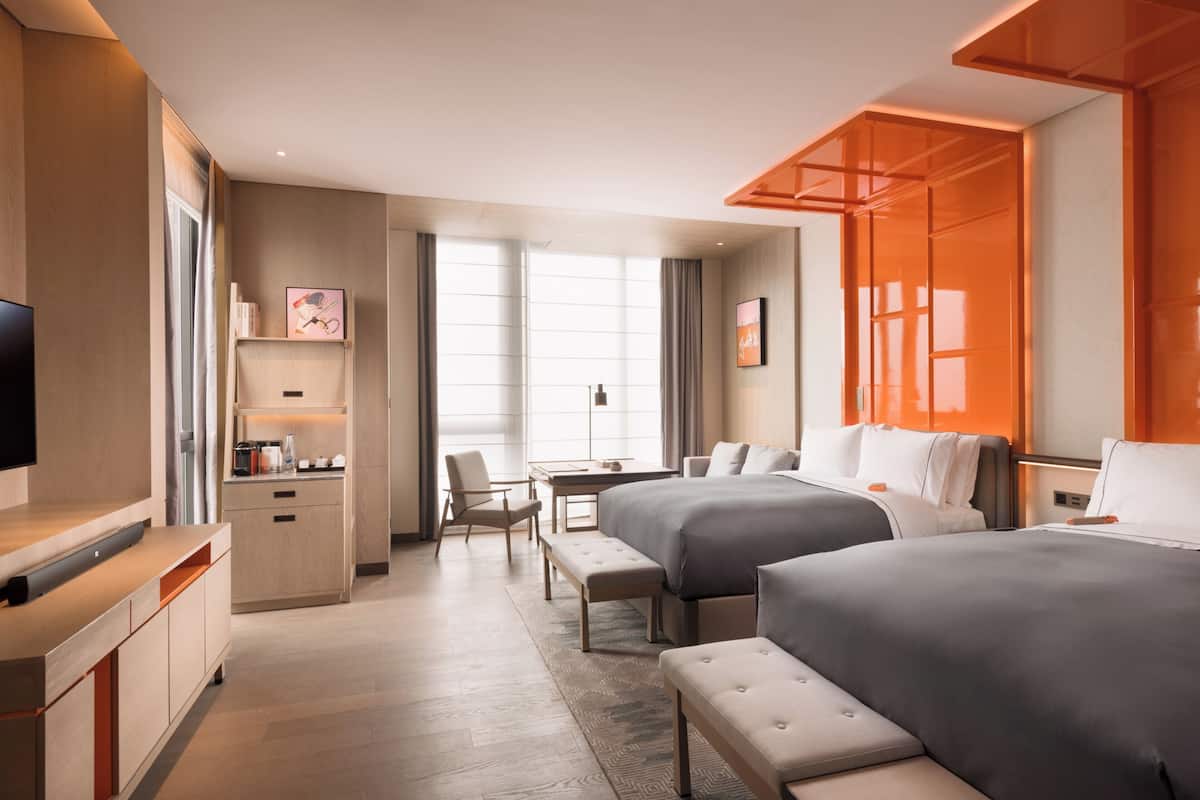 Quarto de hotel com duas camas, uma escrivaninha, uma cadeira, televisão e minibar.