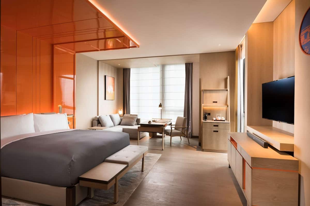 Quarto de hotel moderno com uma cama grande, um sofá, uma escrivaninha e uma televisão.