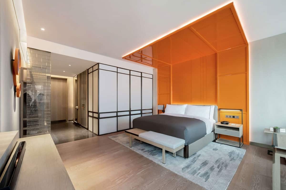 Quarto moderno com uma cama grande, um banquinho, uma mesa de cabeceira e um guarda-roupa.