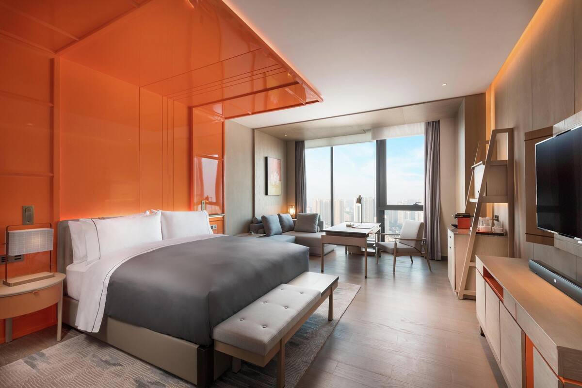 Quarto de hotel moderno com uma cama grande, uma escrivaninha, televisão de tela plana e varanda com vista para a cidade.