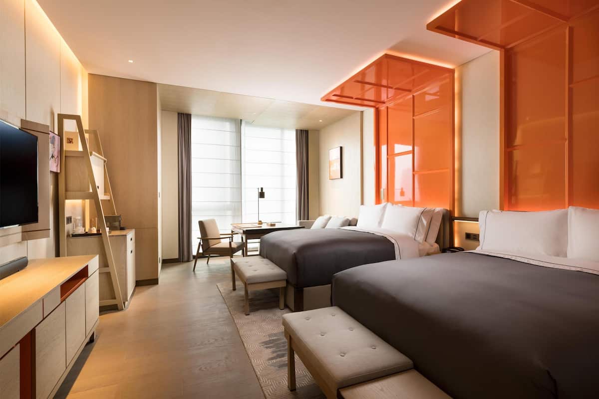 Quarto de hotel com duas camas, uma escrivaninha, uma televisão e uma escada.