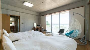 Quarto de hotel com duas camas, uma escrivaninha, uma cadeira e uma janela grande com vista.