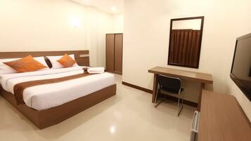 Quarto de hotel com cama, escrivaninha, cadeira, televisão e guarda-roupa.