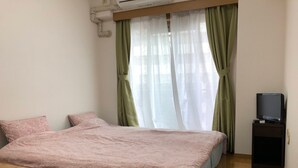 Quarto com cama, televisão sobre um suporte e janela com cortinas.
