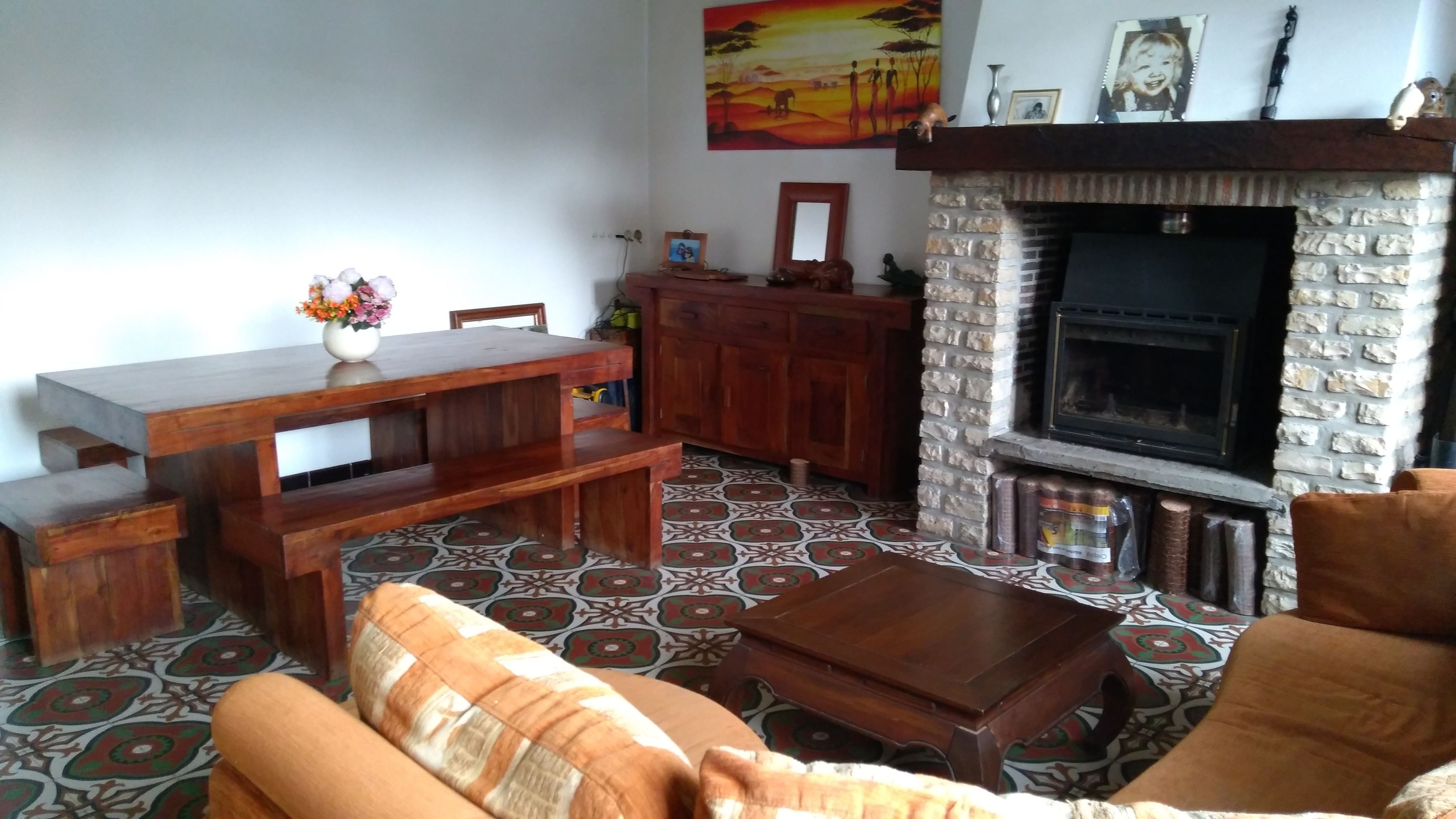 Uma sala de estar com lareira, piso estampado, móveis de madeira e um quadro na parede.