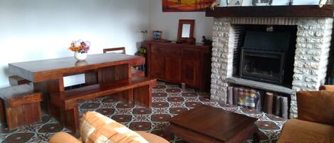 Uma sala de estar com lareira, piso estampado, móveis de madeira e um quadro na parede.