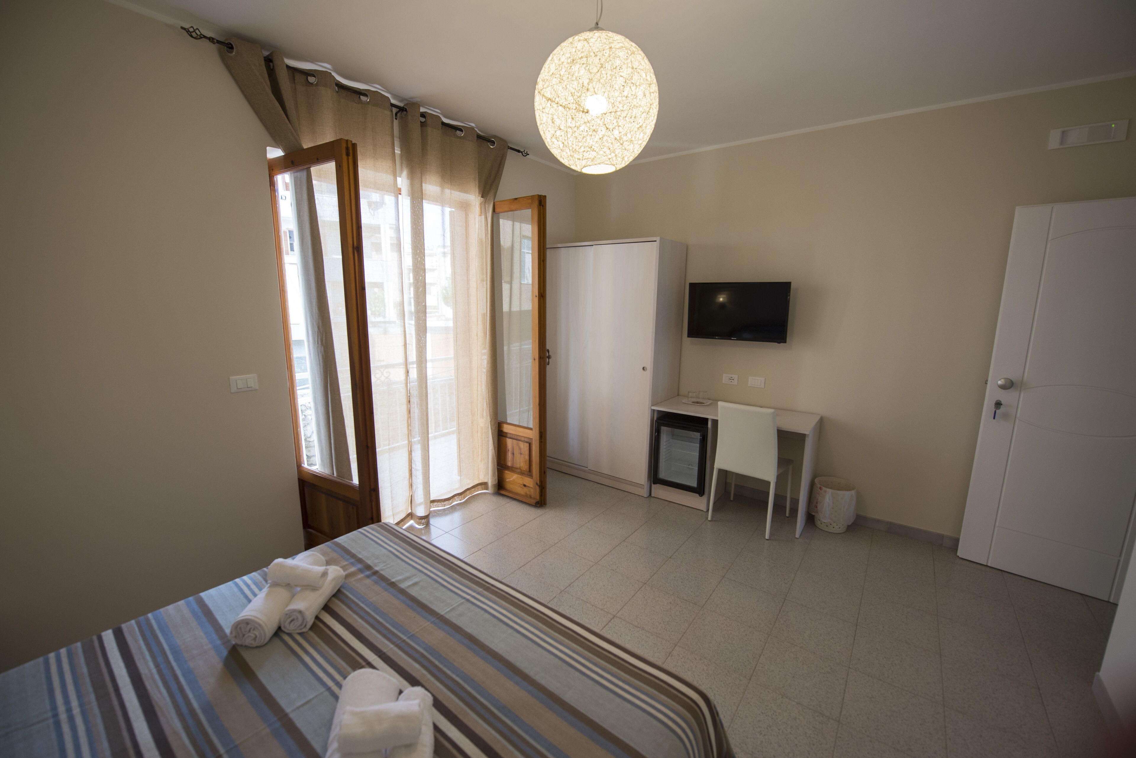 Quarto de hotel com cama, secretária, televisão e guarda-roupa.