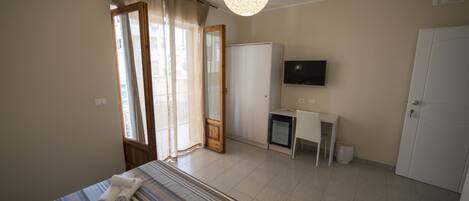 Quarto de hotel com cama, secretária, televisão e guarda-roupa.