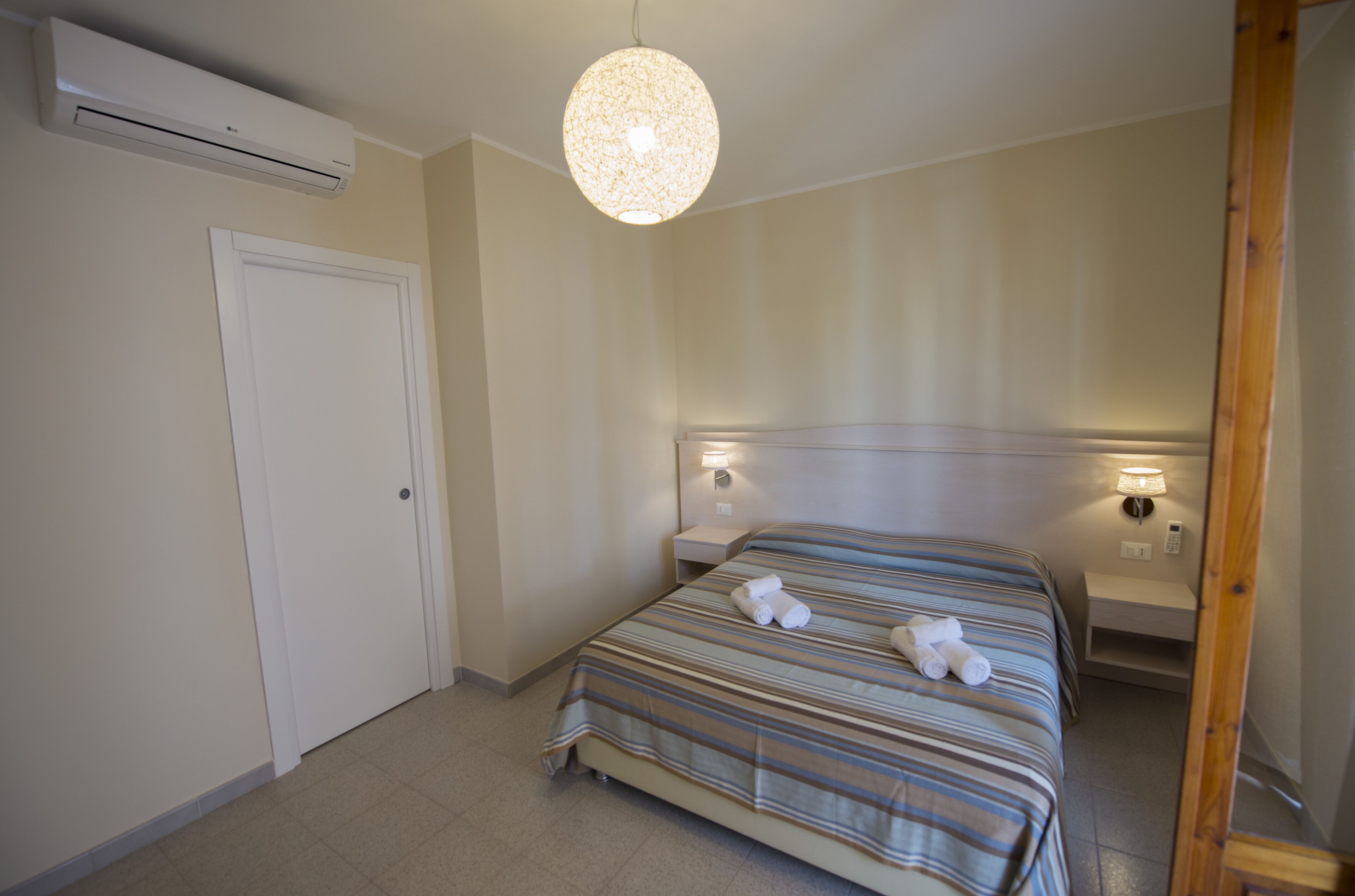 Quarto de hotel com cama, luminárias de cabeceira, porta e ar condicionado.
