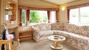 Uma sala de estar acolhedora com um sofá floral, uma mesa de centro redonda e uma grande janela com cortinas.