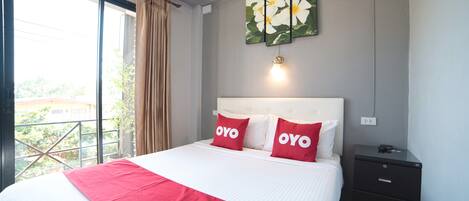Quarto de hotel com cama, mesa de cabeceira, janela com cortinas e luminária na parede.