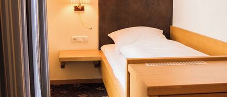 Quarto de hotel com cama, mesa de cabeceira, abajur e carpete estampado.