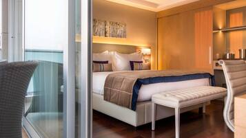 Quarto de hotel moderno com uma cama grande, uma mesinha de cabeceira, uma cadeira e vista através de uma porta de vidro.