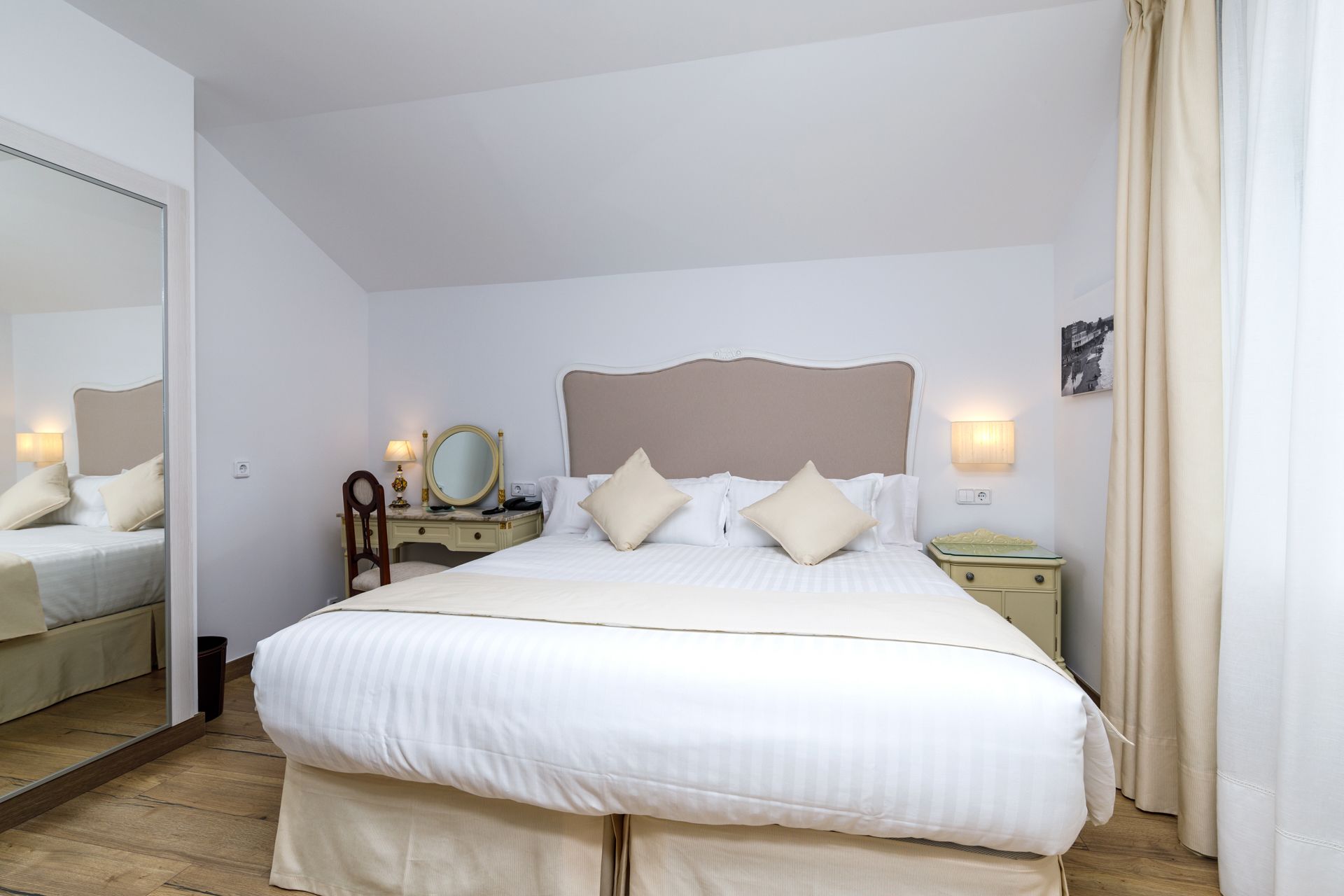 Quarto bem arrumado com uma cama grande, mesa de cabeceira com abajur, espelho e um criado-mudo.