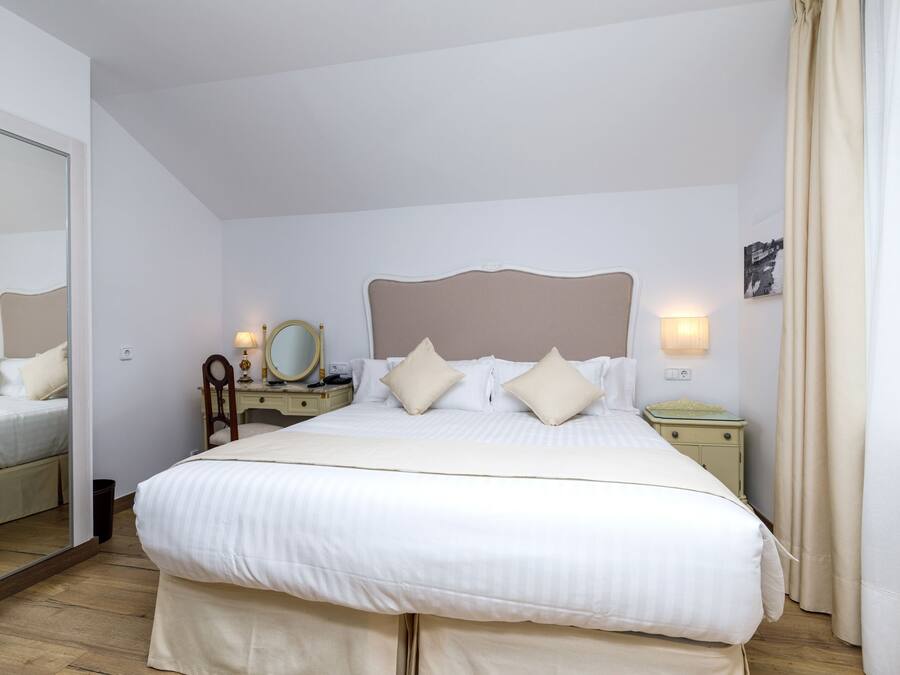 Quarto bem arrumado com uma cama grande, mesa de cabeceira com abajur, espelho e um criado-mudo.