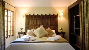 Quarto de hotel com uma cama grande, duas mesas de cabeceira, uma luminária e um painel de cabeceira de madeira, além de uma janela com cortinas.