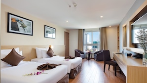 Quarto de hotel com duas camas, uma escrivaninha, uma cadeira e vista para a cidade.