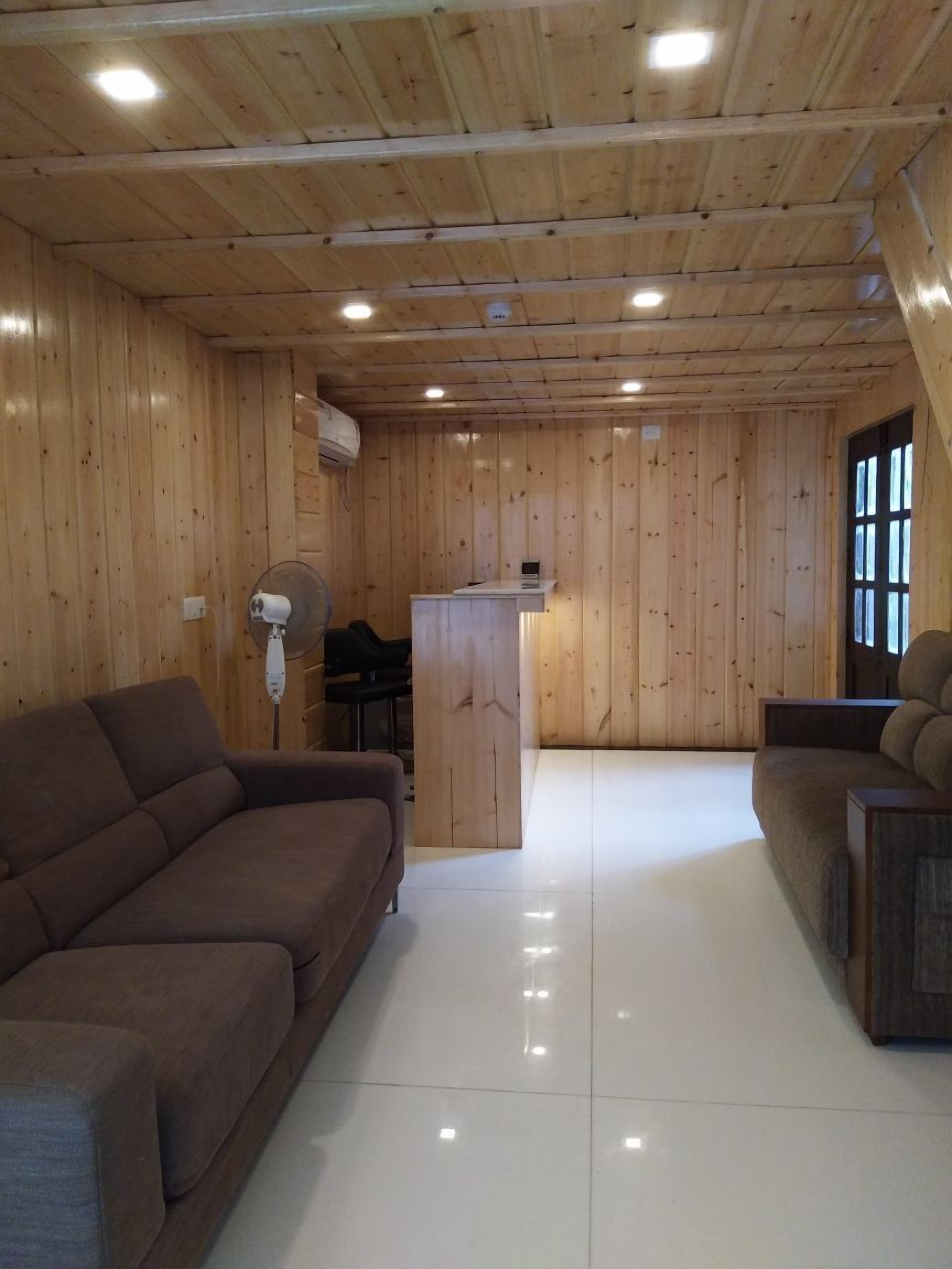 Interior em madeira com sofá, ventoinha e uma pequena mesa.