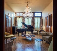 Uma sala de estar ampla com um piano de cauda, assentos confortáveis, um lustre e grandes janelas com cortinas.