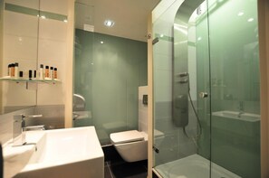 Uma casa de banho moderna com cabine de duche em vidro, lavatório branco e sanita.
