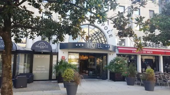 Um hotel com placa chamativa, área de estar ao ar livre e plantas em vasos.