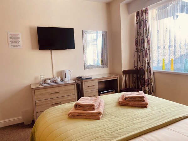 Quarto de hotel com cama, escrivaninha, cadeira, televisão e janela com cortinas.