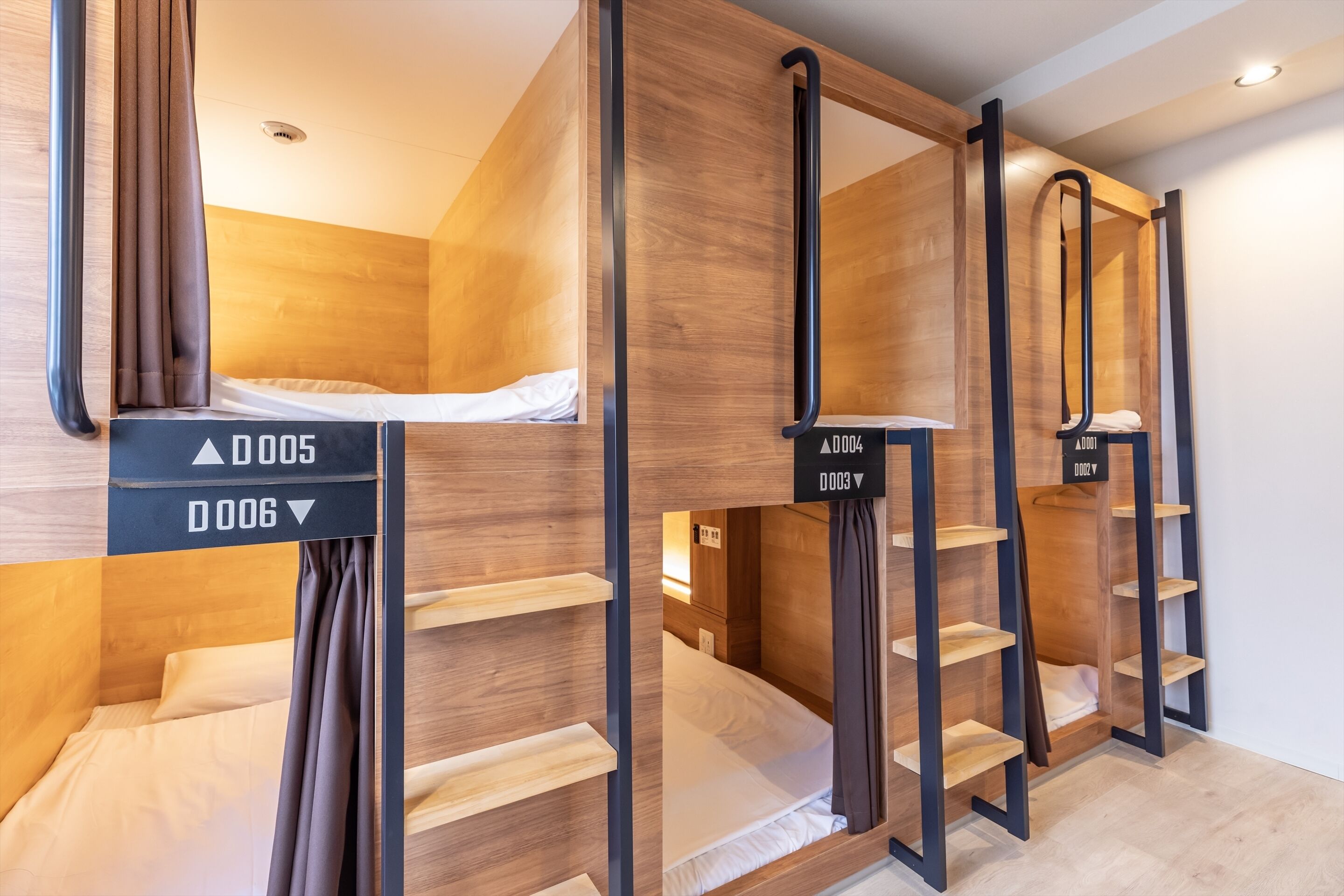 Quarto de hotel moderno com beliches identificados como D005, D006 e D007.
