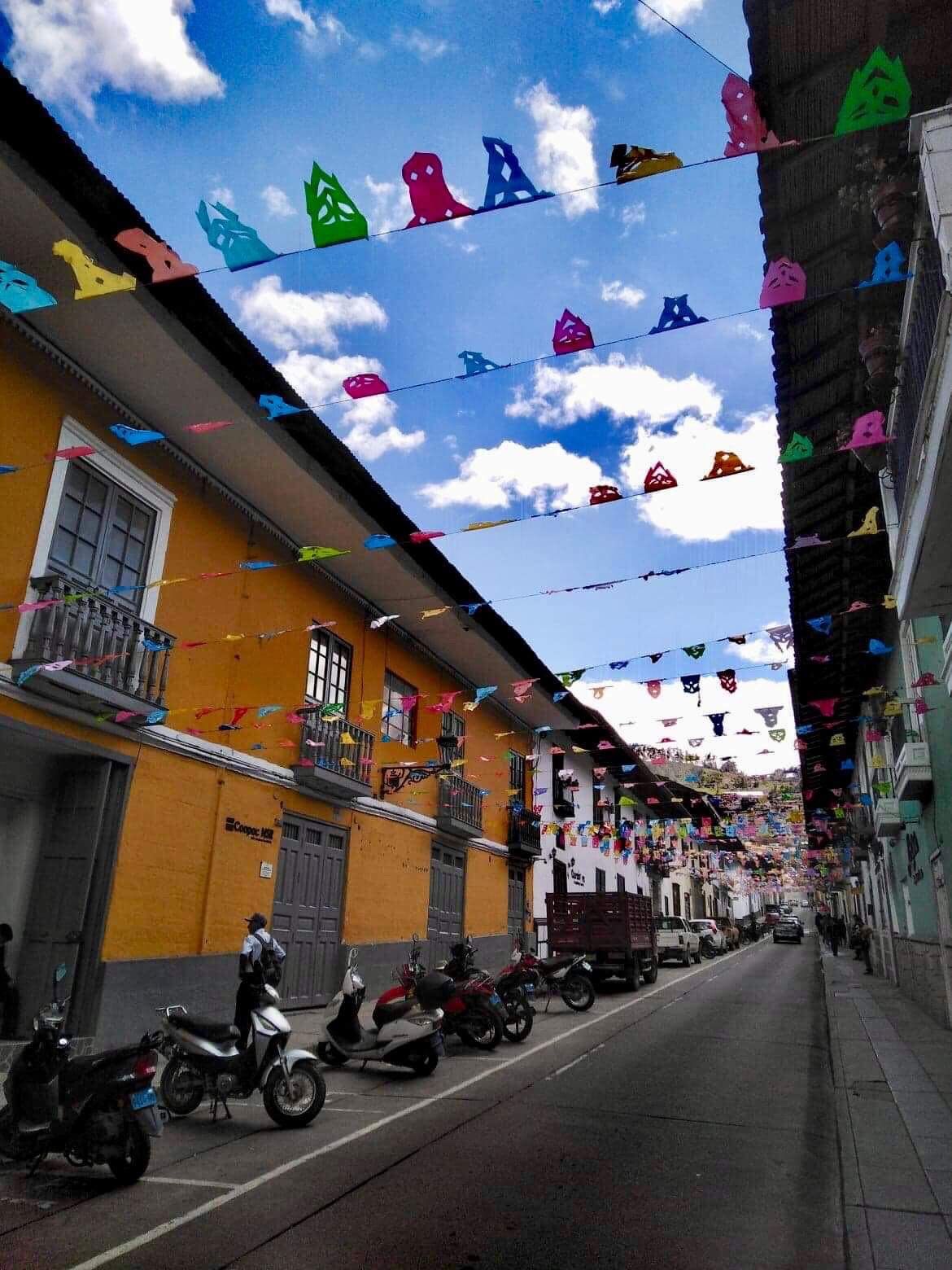 Rua com scooters estacionadas e bandeirinhas coloridas triangulares.