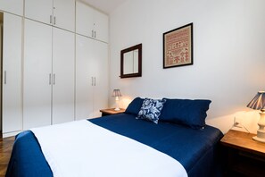 Quarto com cama, mesas de cabeceira, guarda-roupa e espelho fixado na parede.