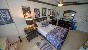 Um quarto com cama, mesas de cabeceira, cômoda, ventoinha no teto e quadros nas paredes.