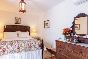 Quarto de hotel com cama, luminárias de cabeceira, cômoda, espelho e um quadro na parede.