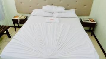 Uma cama bem arrumada com cabeceira estofada, duas mesas de cabeceira com um telefone e um livro, e um pequeno banco à esquerda.