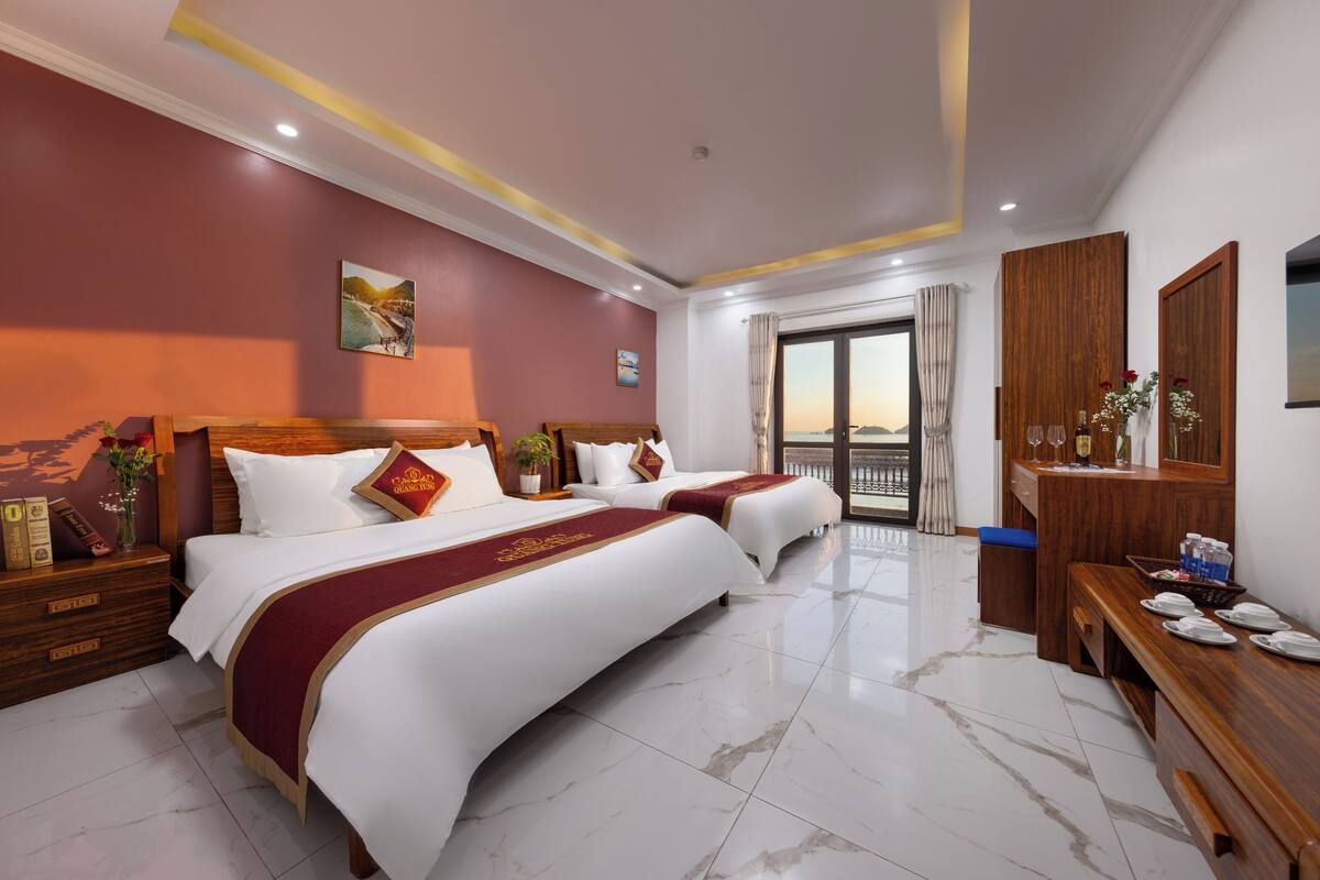 Quarto de hotel com duas camas, uma escrivaninha de madeira, varanda com vista e um espelho grande.