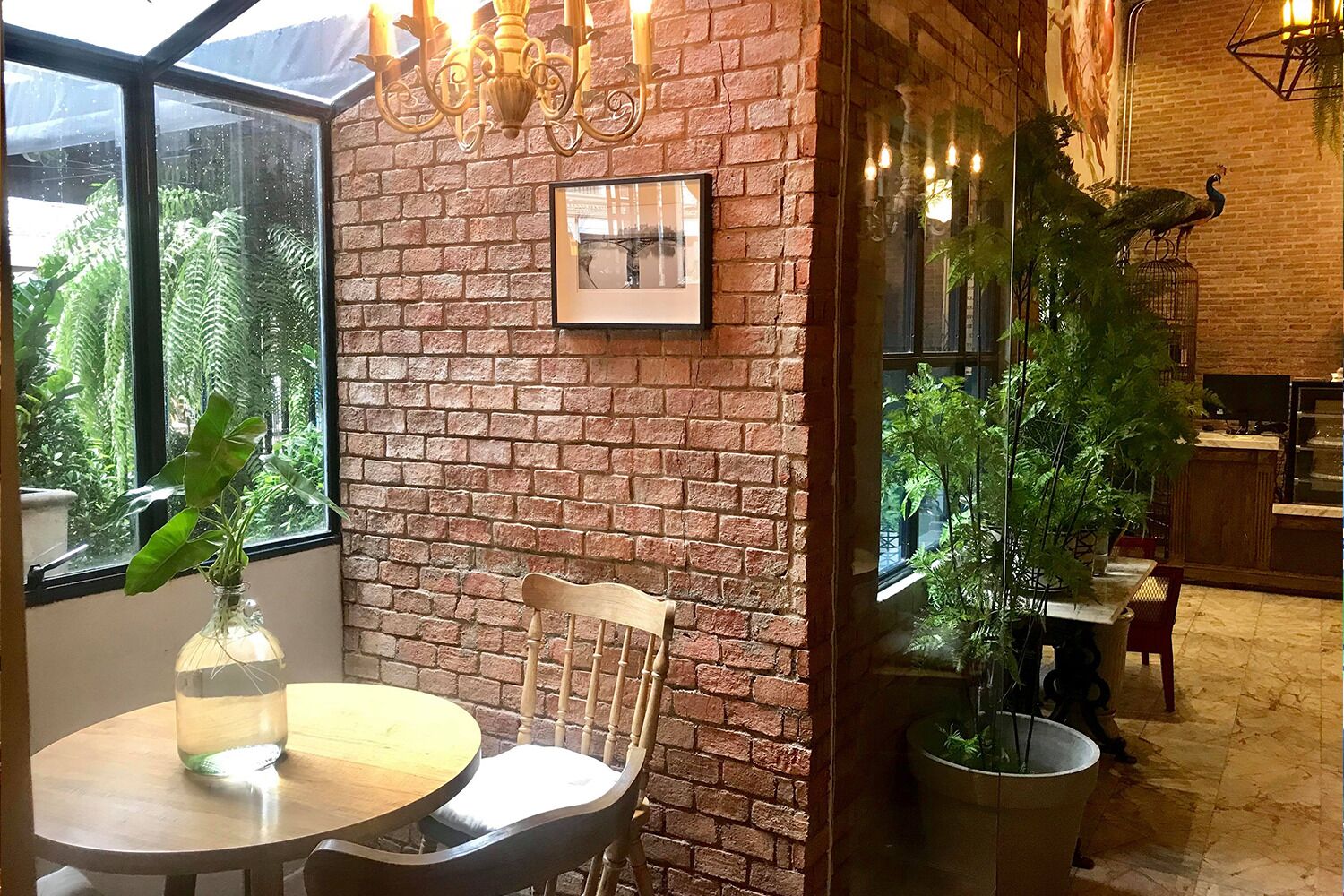 Paredes de tijolo com um quadro emoldurado, uma cadeira de madeira, uma mesa redonda com um vaso de plantas verdes e um vaso de planta.