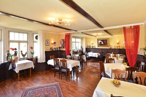Uma sala de jantar com várias mesas e cadeiras, piso de madeira e cortinas vermelhas.