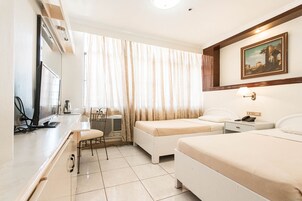 Quarto de hotel com duas camas, uma escrivaninha com cadeira, televisão e um quadro na parede.